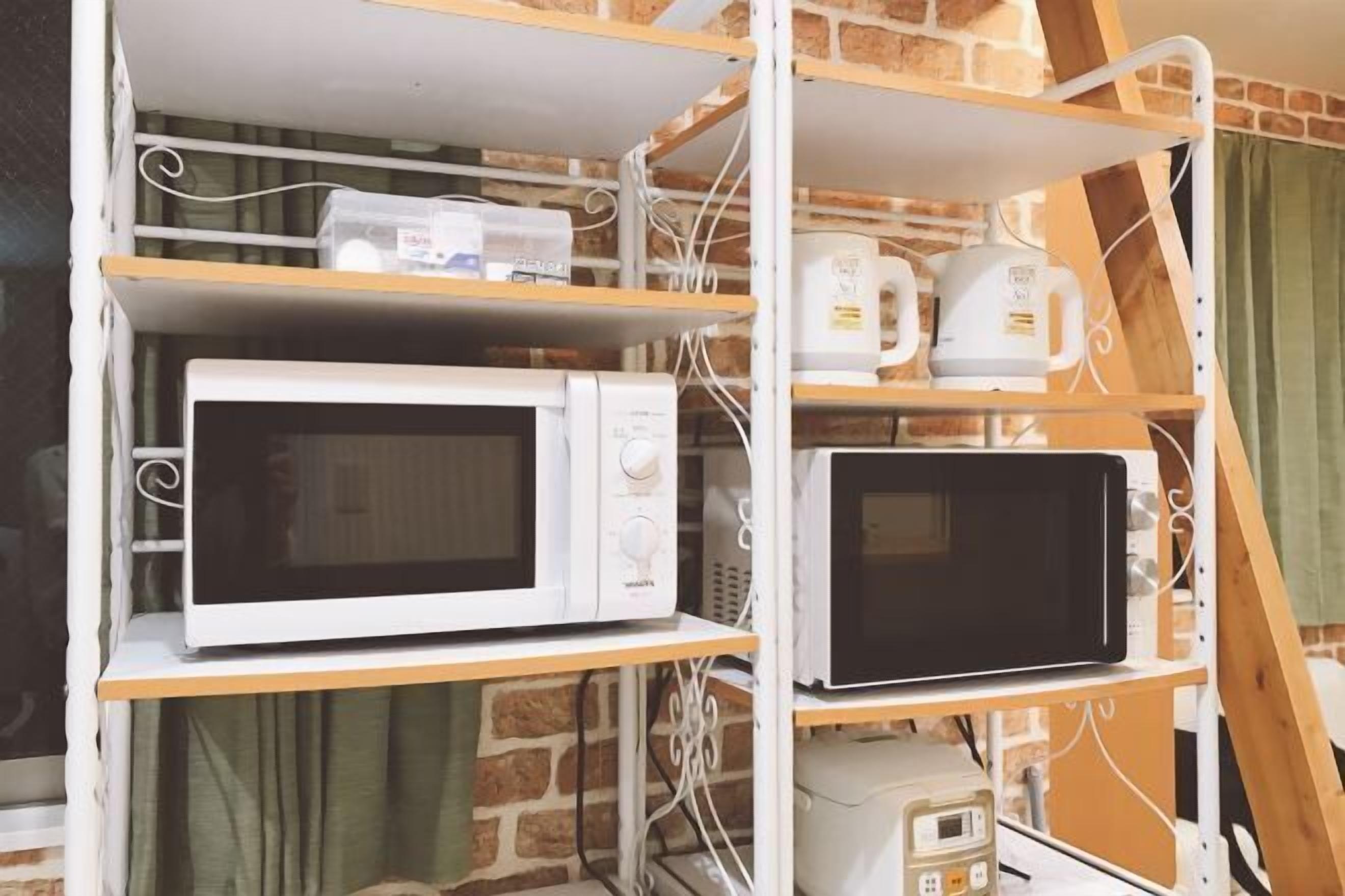 Uma área de cozinha com duas micro-ondas em prateleiras, uma cafeteira e um eletrodoméstico na prateleira inferior.