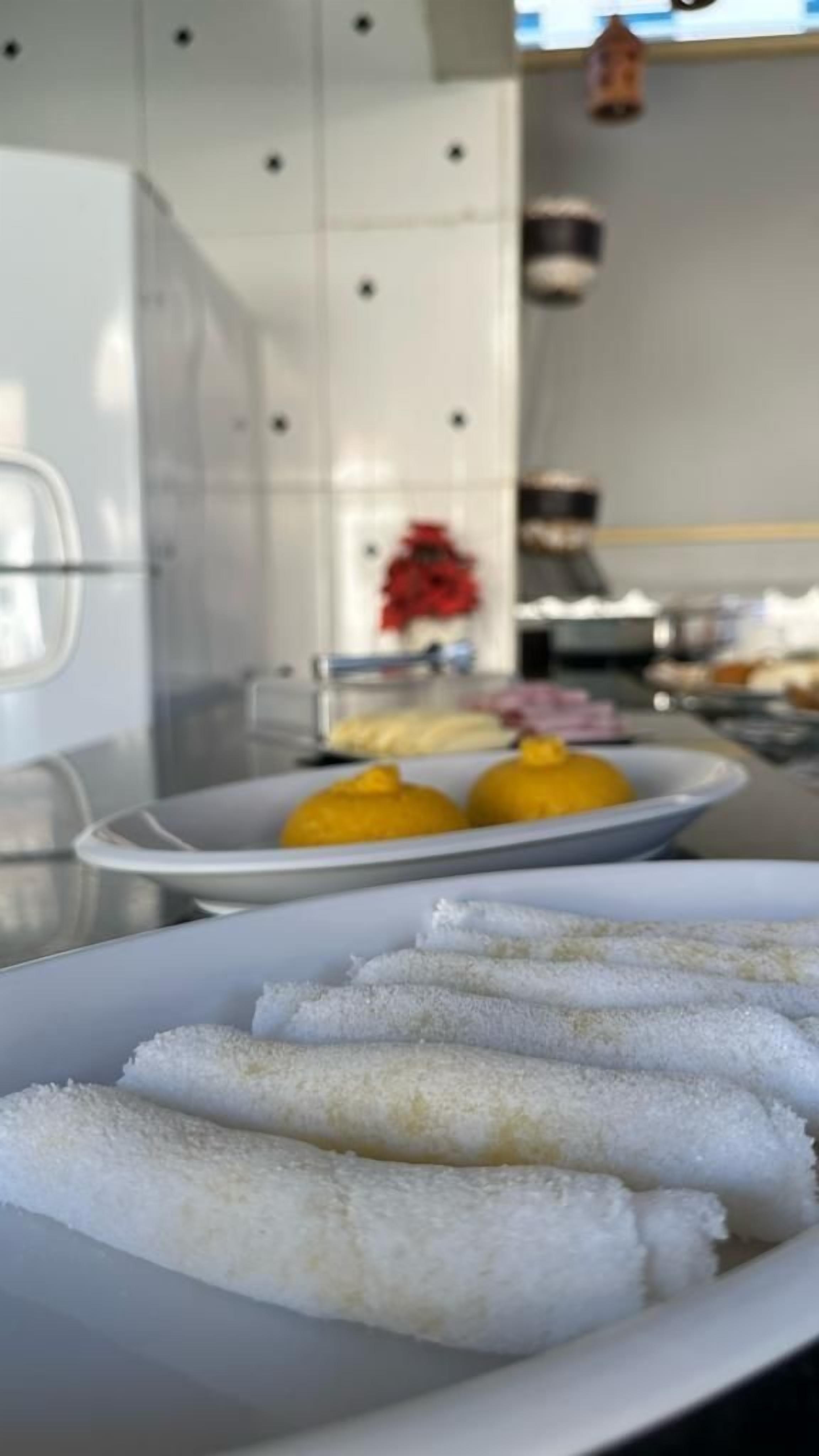 Cozinha com armários e bancada brancos. Há limões numa travessa e um prato branco com alimentos.