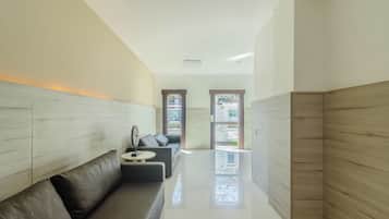 Um interior moderno com um sofá, uma mesinha e um ventilador. Vê-se uma paisagem através de uma porta.