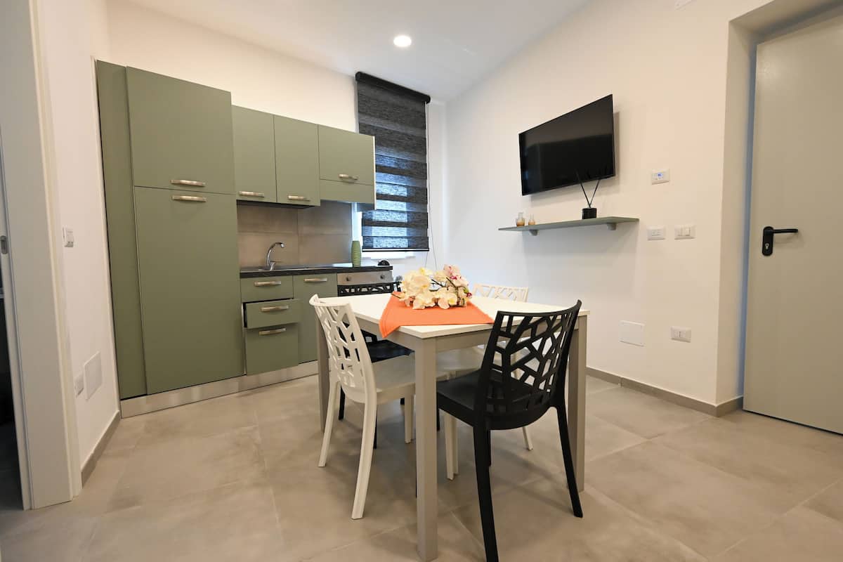 Uma cozinha compacta com armários verdes, uma mesa de jantar branca e uma cadeira preta.