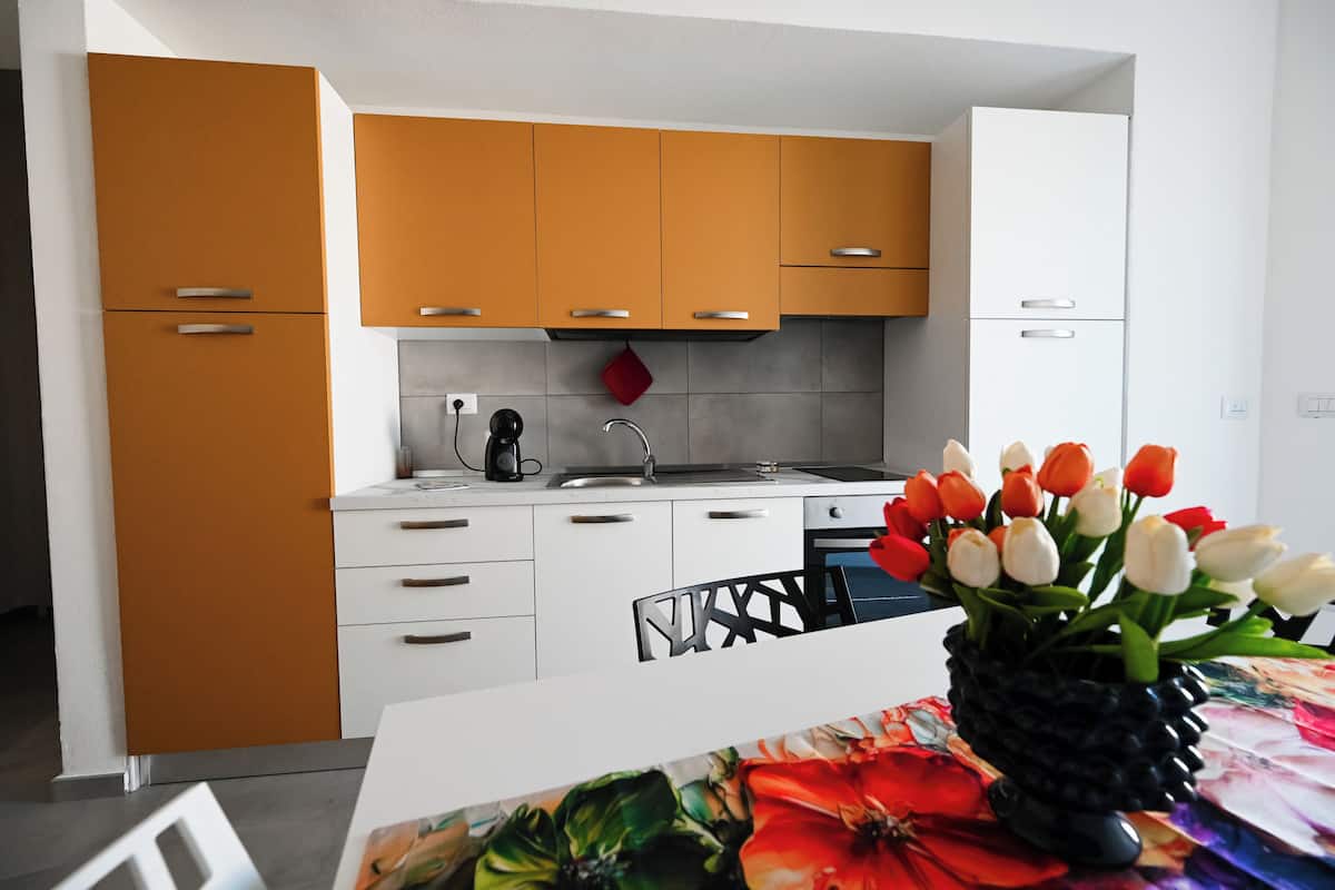 Uma cozinha moderna com armários brancos e laranja, uma pia de aço inoxidável e um vaso decorativo com tulipas.