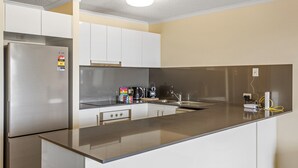 Cozinha moderna com armários brancos, eletrodomésticos de aço inoxidável e bancada de granito.