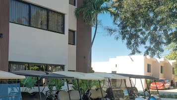 Uma fileira de carrinhos de golfe estacionados em frente a um edifício com janelas amplas e uma árvore.