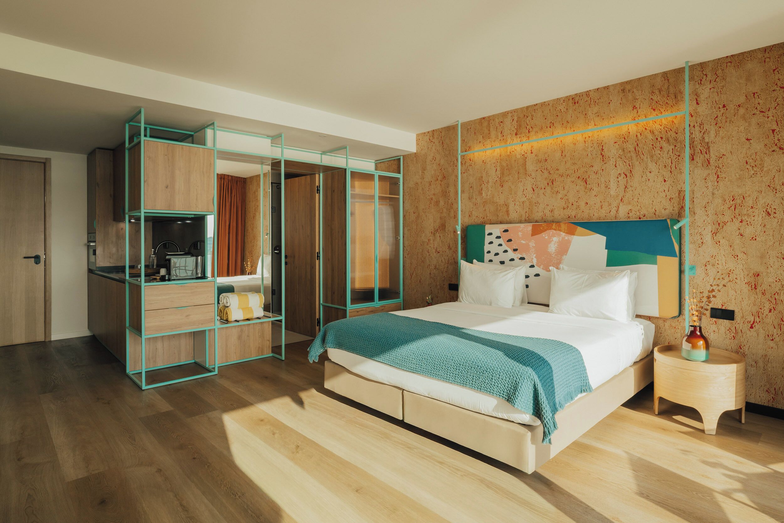 Quarto de hotel com cama, mesa de cabeceira, guarda-roupa aberto e banheiro visível.