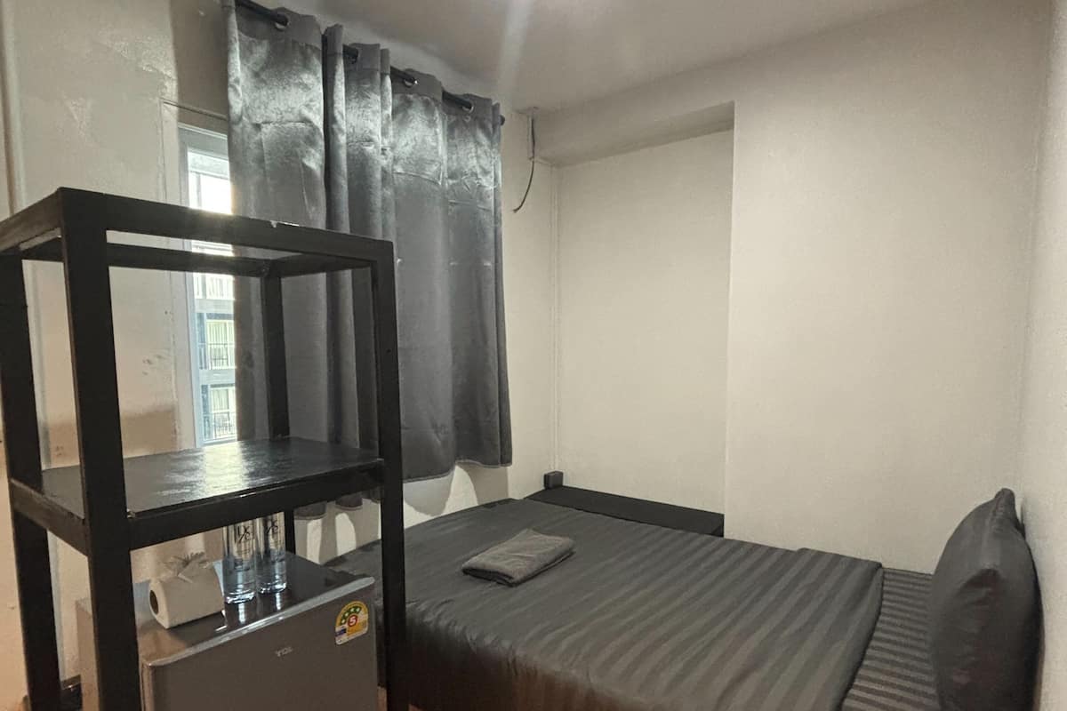Quarto compacto com cama, uma pequena escrivaninha e um frigorífico.