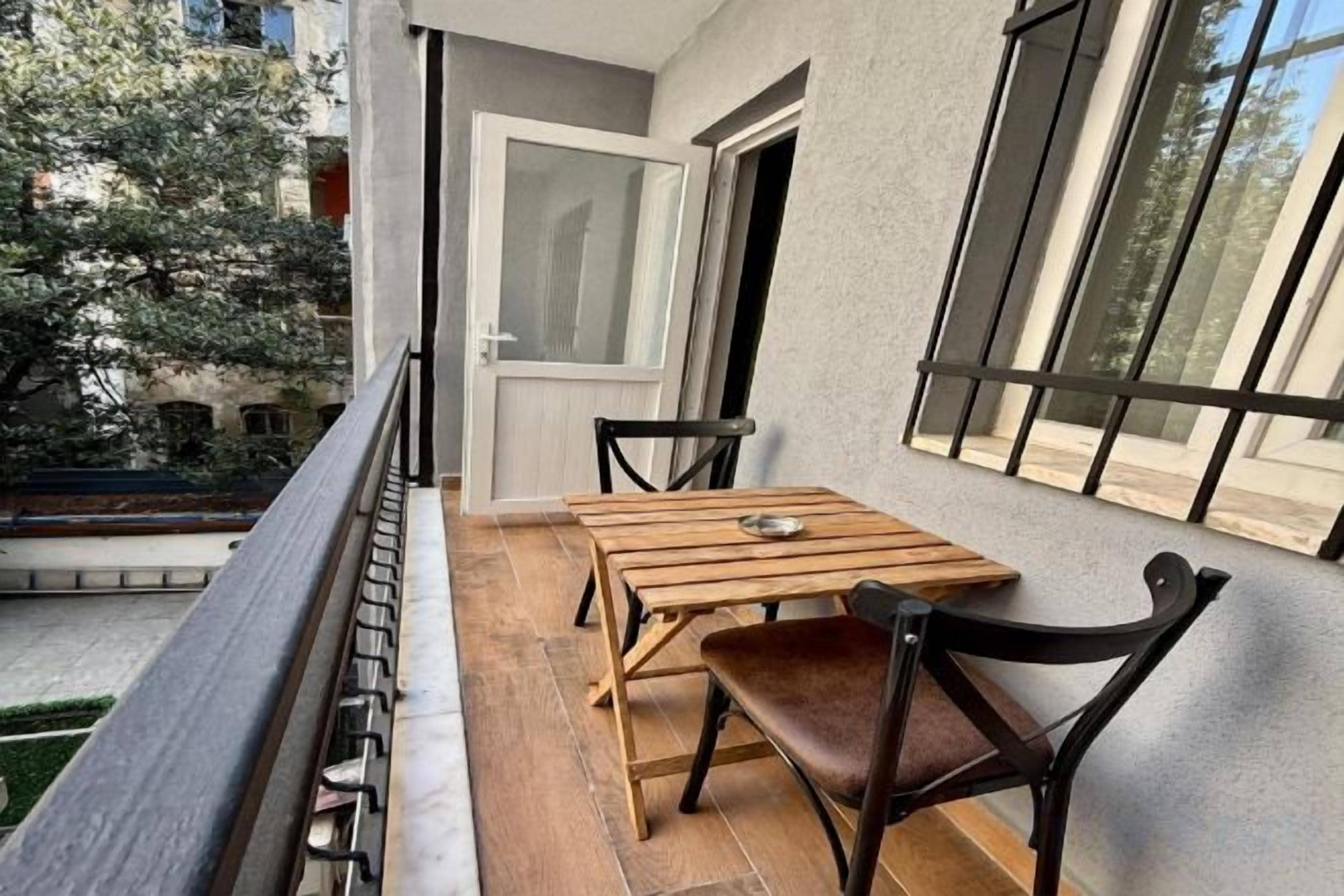 Uma varanda com uma mesa de madeira e duas cadeiras, uma porta e vista para o exterior.
