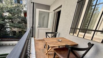 Uma varanda com uma mesa de madeira e duas cadeiras, uma porta e vista para o exterior.