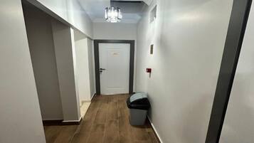 Corredor estreito com uma porta no final, uma lixeira e uma luminária no teto.