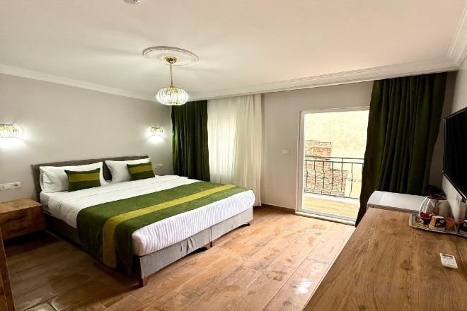 Quarto de hotel com cama, escrivaninha de madeira, televisão e varanda com cortinas.