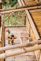 Escada de bambu que leva a uma plataforma com uma mesa, onde há um vaso com flores e bules.