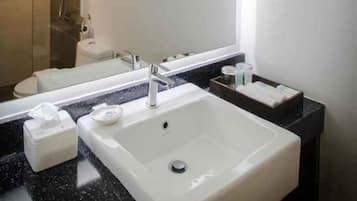 Casa de banho com lavatório branco, espelho e bancada preta.