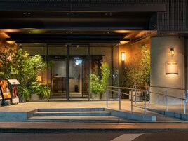 Entrada de um edifício moderno com portas de vidro, escadas e plantas.