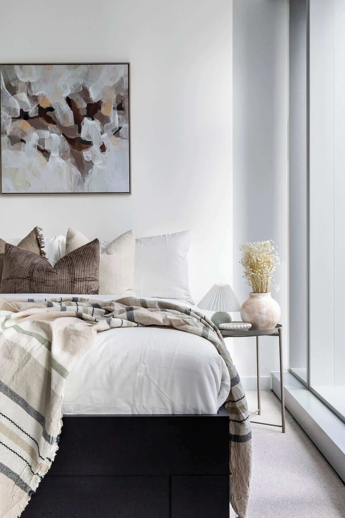 Um quarto moderno com uma cama grande, uma mesinha de cabeceira com um vaso e uma janela com vista.