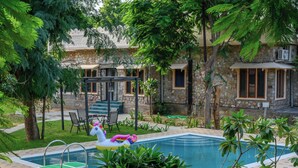 Piscina com flutuador de unicórnio, rodeada por vegetação exuberante e edifícios de pedra.