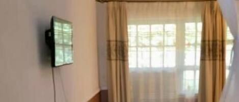 Quarto com uma cama, televisão na parede e janela com cortinas.