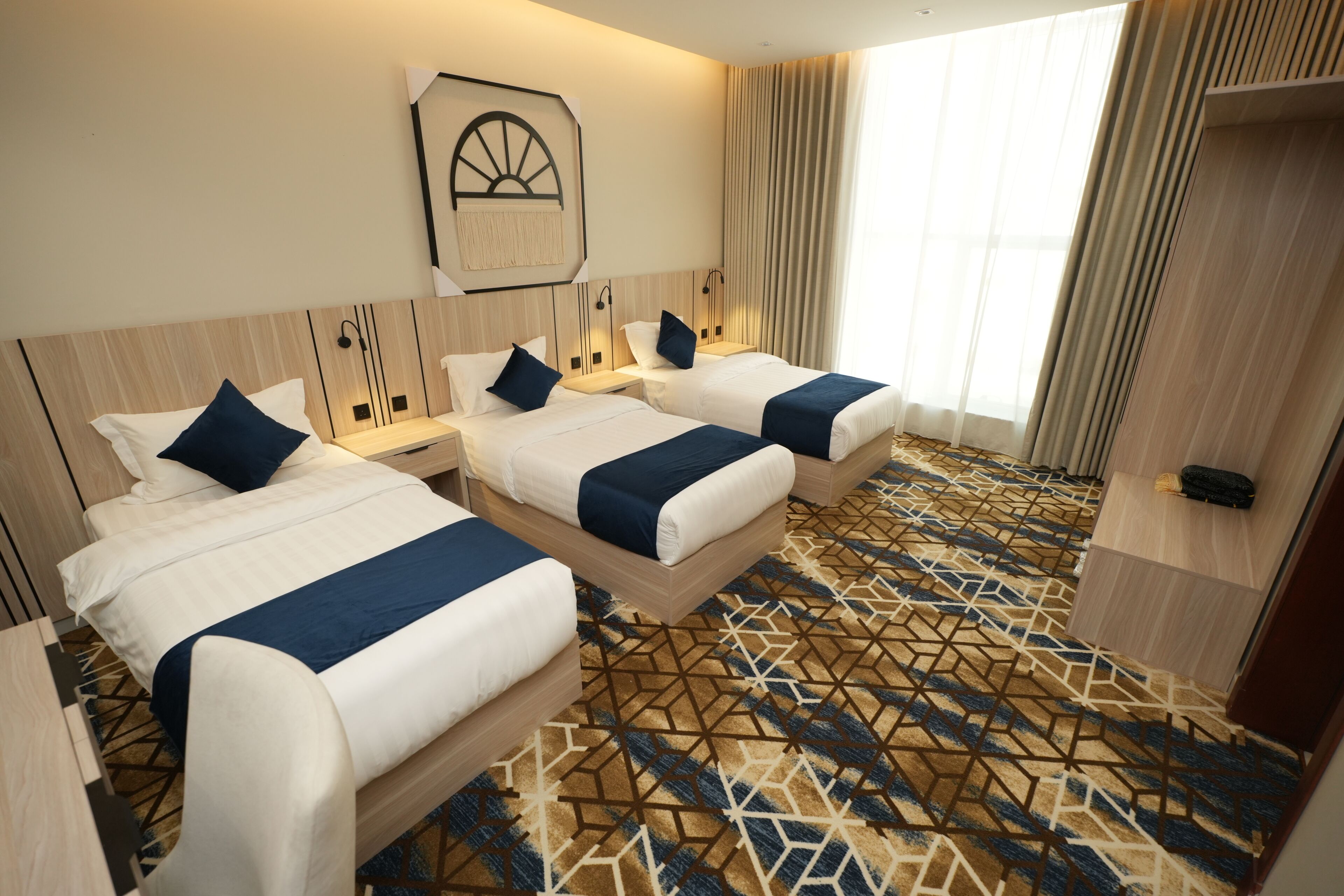 Quarto de hotel com duas camas, carpete estampado, obra de arte na parede e uma janela grande com cortinas.