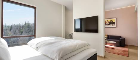 Quarto de hotel moderno com uma cama grande, televisão na parede e vista para a floresta pela janela.