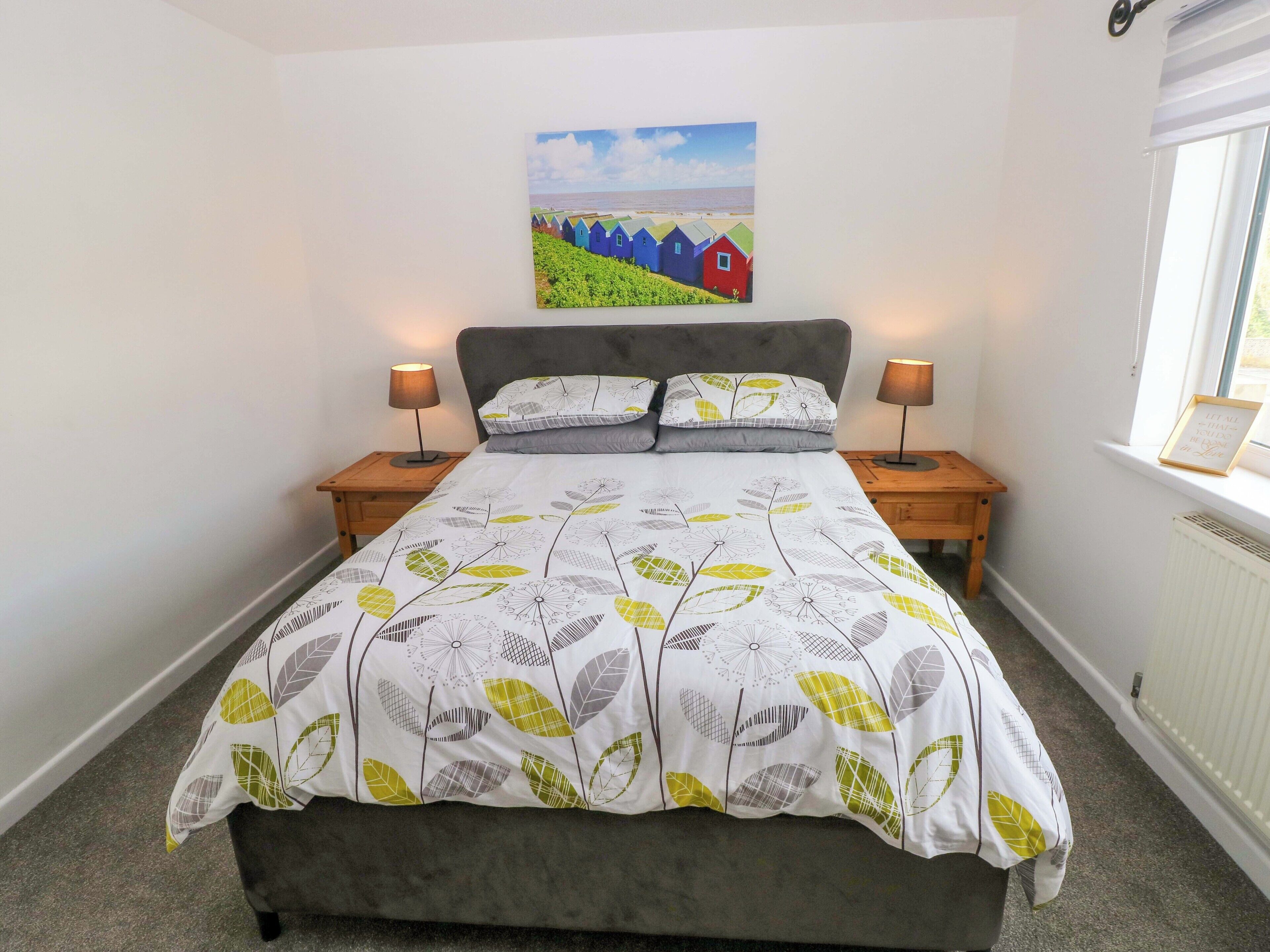Quarto com cama, duas mesas de cabeceira, um quadro sobre a cama e uma janela com vista para a praia.