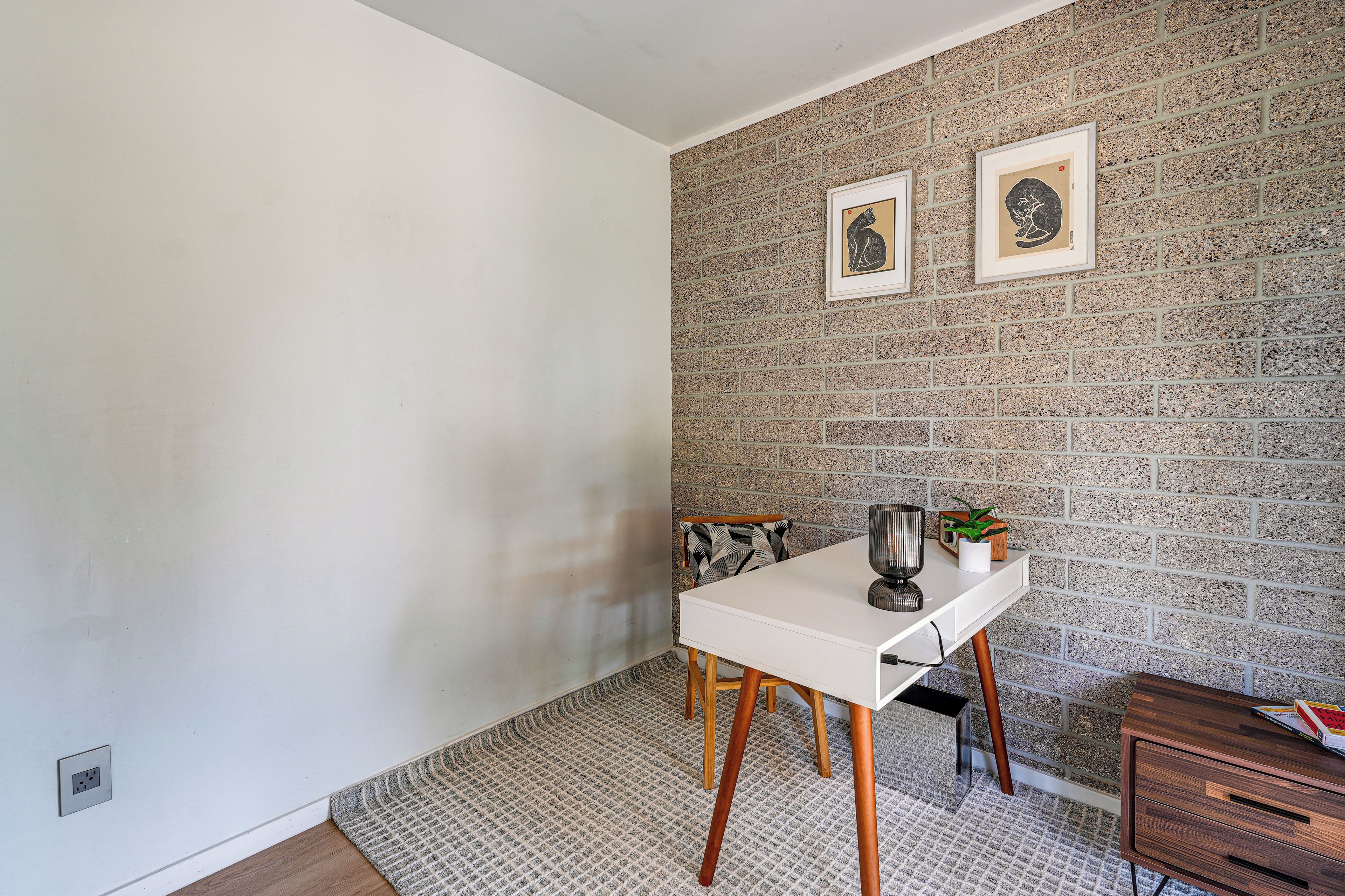 Quarto com mesa branca, duas molduras na parede, uma planta pequena e um armário de madeira.