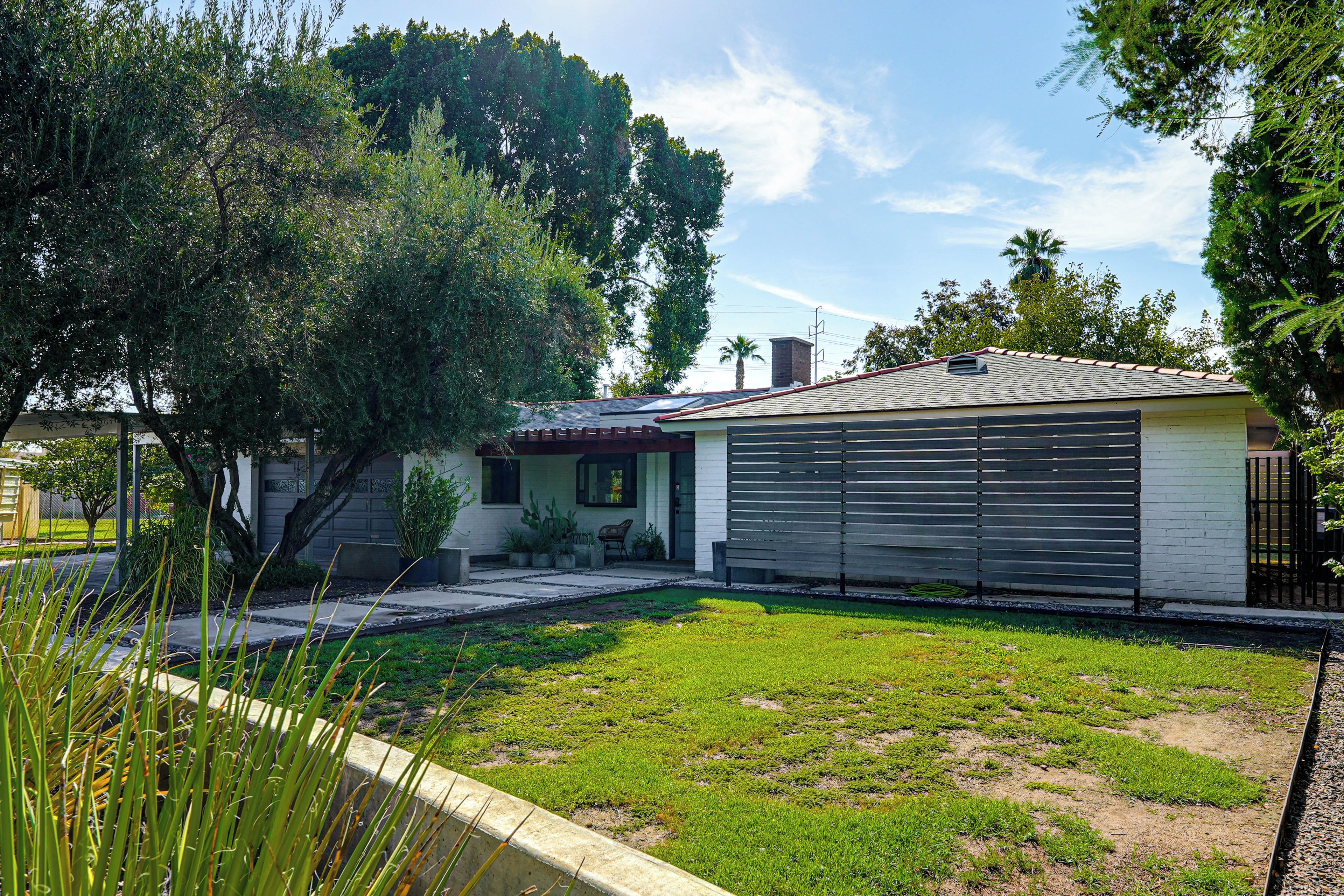 Um imóvel residencial com garagem, gramado frontal e uma grande árvore.