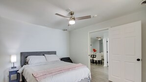 Quarto com cama, mesa de cabeceira, abajur, ventilador de teto e porta para outro cômodo.