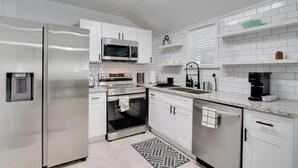 Uma cozinha moderna com eletrodomésticos de aço inoxidável, armários brancos e um tapete com padrão herringbone.