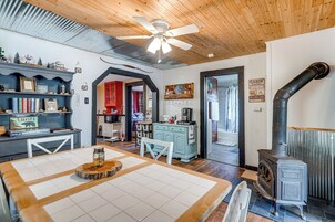 Interior acolhedor de cabana com uma mesa de jantar, um ventilador de teto de madeira, um fogão antigo e uma estante repleta de livros e objetos decorativos.