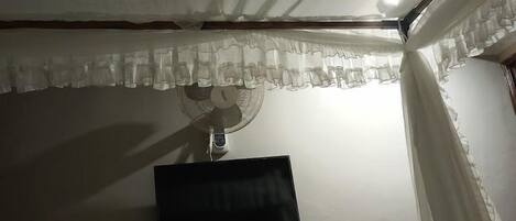 Quarto com uma cama, televisão na parede e ventoinha no teto.