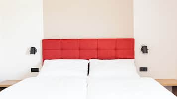 Uma cama com roupa de cama branca, uma cabeceira estofada vermelha e duas luminárias de cabeceira.