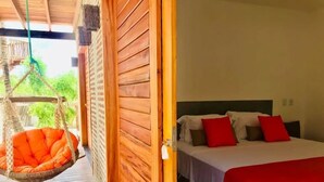 Quarto de madeira com cama, cadeira suspensa e vista para o verde lá fora.