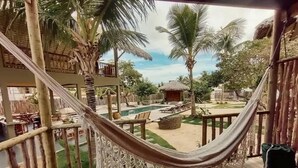 Uma rede sobre um deck de madeira com vista para uma área de piscina, cadeiras de sol e palmeiras.