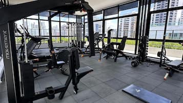 Uma academia moderna com diversos equipamentos de exercício, janelas amplas e vista para a paisagem urbana.