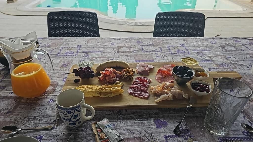 Uma mesa com diversos alimentos, um jarro de suco de laranja e um copo de água.