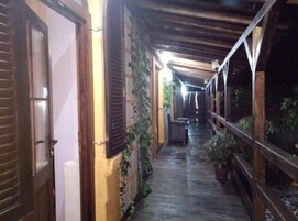 Um corredor estreito com portas e persianas de madeira, um banco de madeira e plantas em vasos.