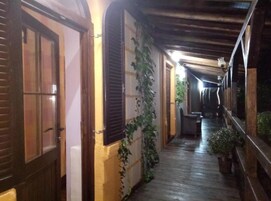 Um corredor estreito com portas e persianas de madeira, chão de azulejos e vasos de plantas.