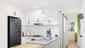 Uma cozinha moderna com armários brancos, uma geladeira preta, uma mesa de madeira e luminárias pendentes.