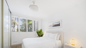 Quarto com cama, mesa de cabeceira e janela com persianas.