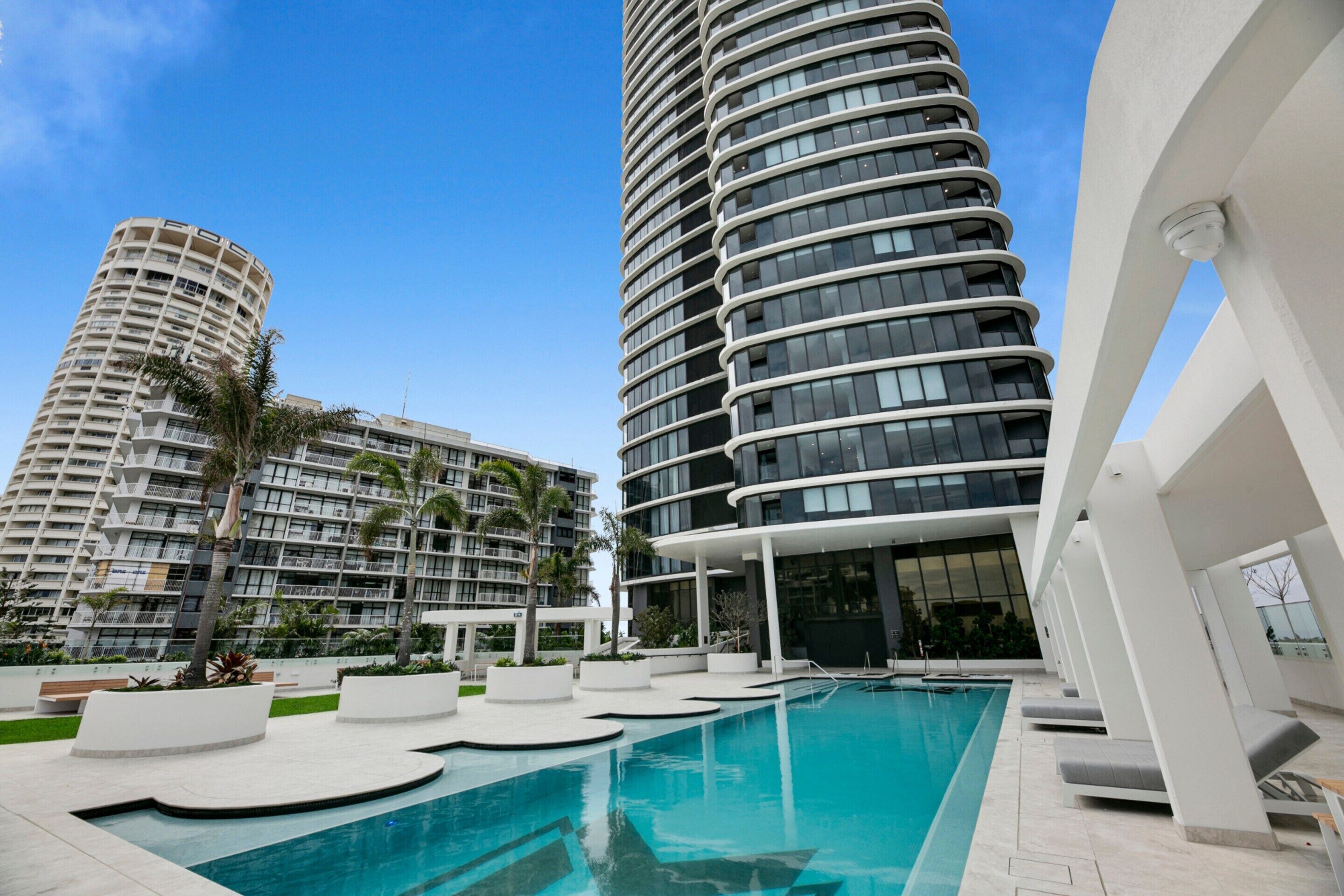 Um hotel moderno com piscina no terraço, cercado por edifícios altos e palmeiras.