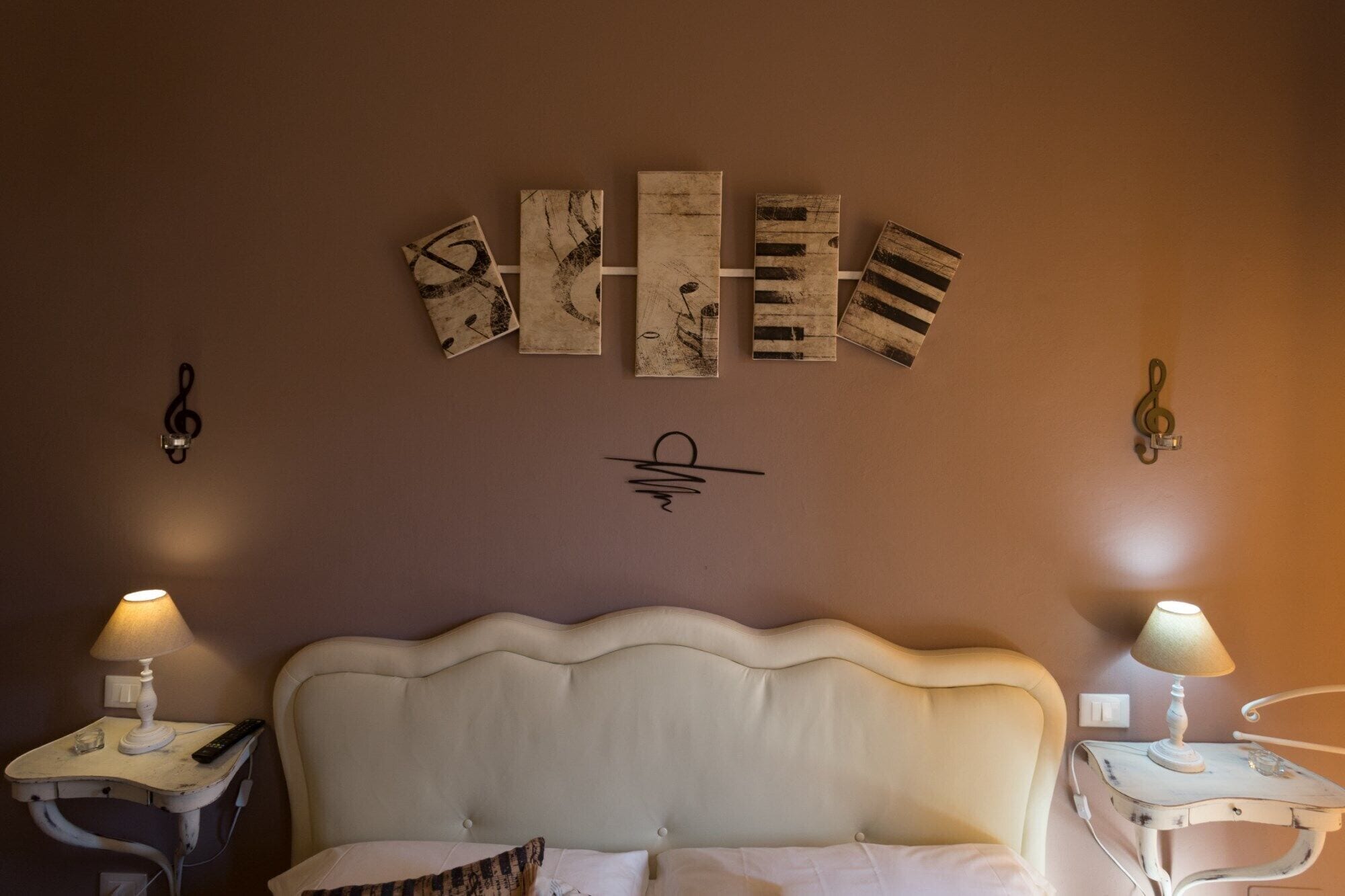 Quarto com cama, duas mesas de cabeceira, luminária na parede e uma obra de arte acima da cama.