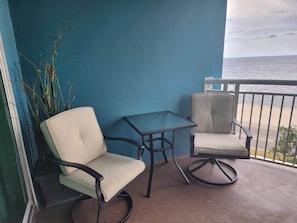 Varanda com duas cadeiras e uma mesa, vista para o oceano, e uma parede azul.
