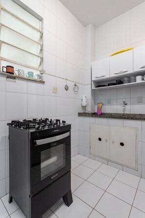 Uma cozinha com paredes revestidas de azulejos brancos, um fogão preto e um forno branco.