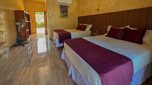 Quarto de hotel com duas camas, cabeceira de madeira, um ventilador e vista para o verde lá fora.