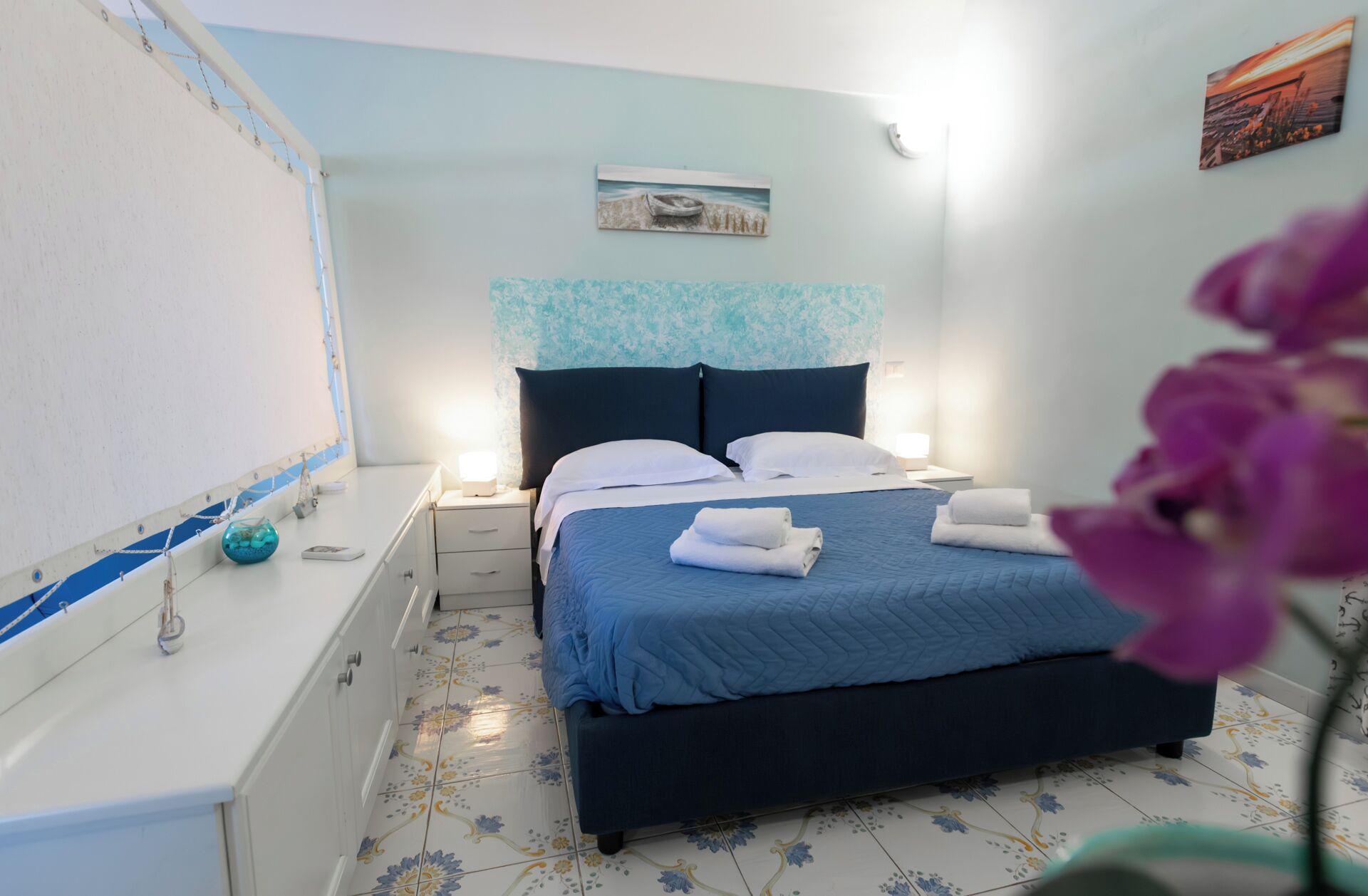 Quarto de hotel bem organizado, com uma cama, mesas de cabeceira, um criado-mudo, um quadro na parede e um chão com padrão floral.