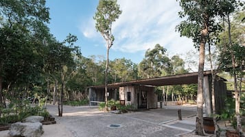 Um edifício rústico com varanda e acesso coberto, rodeado por árvores e caminhos de cascalho.