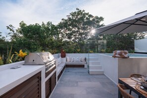 Um pátio externo com churrasqueira, área de estar e vista para árvores.