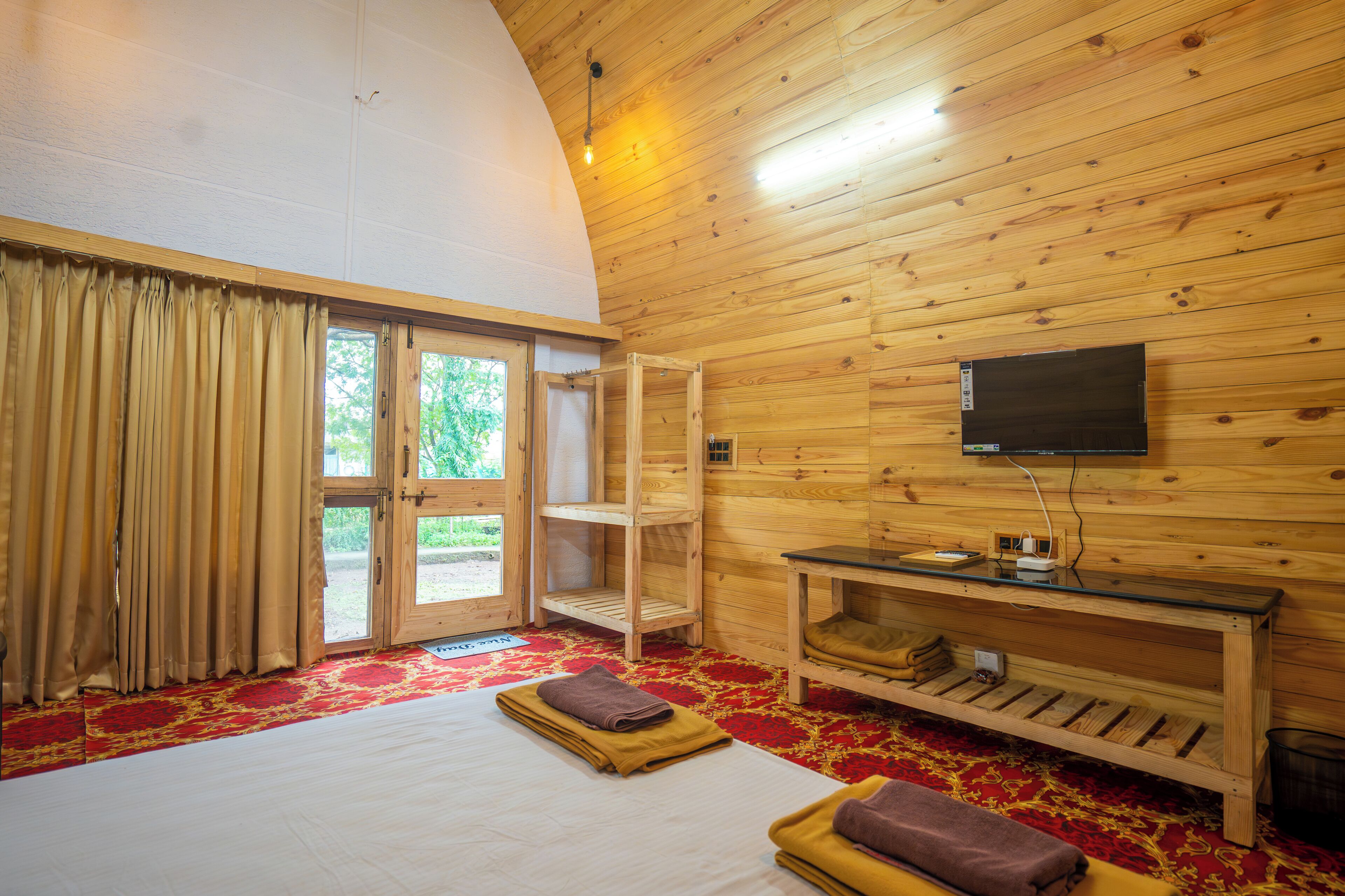 Quarto com cama, um banco de madeira, uma TV e janela com cortinas.