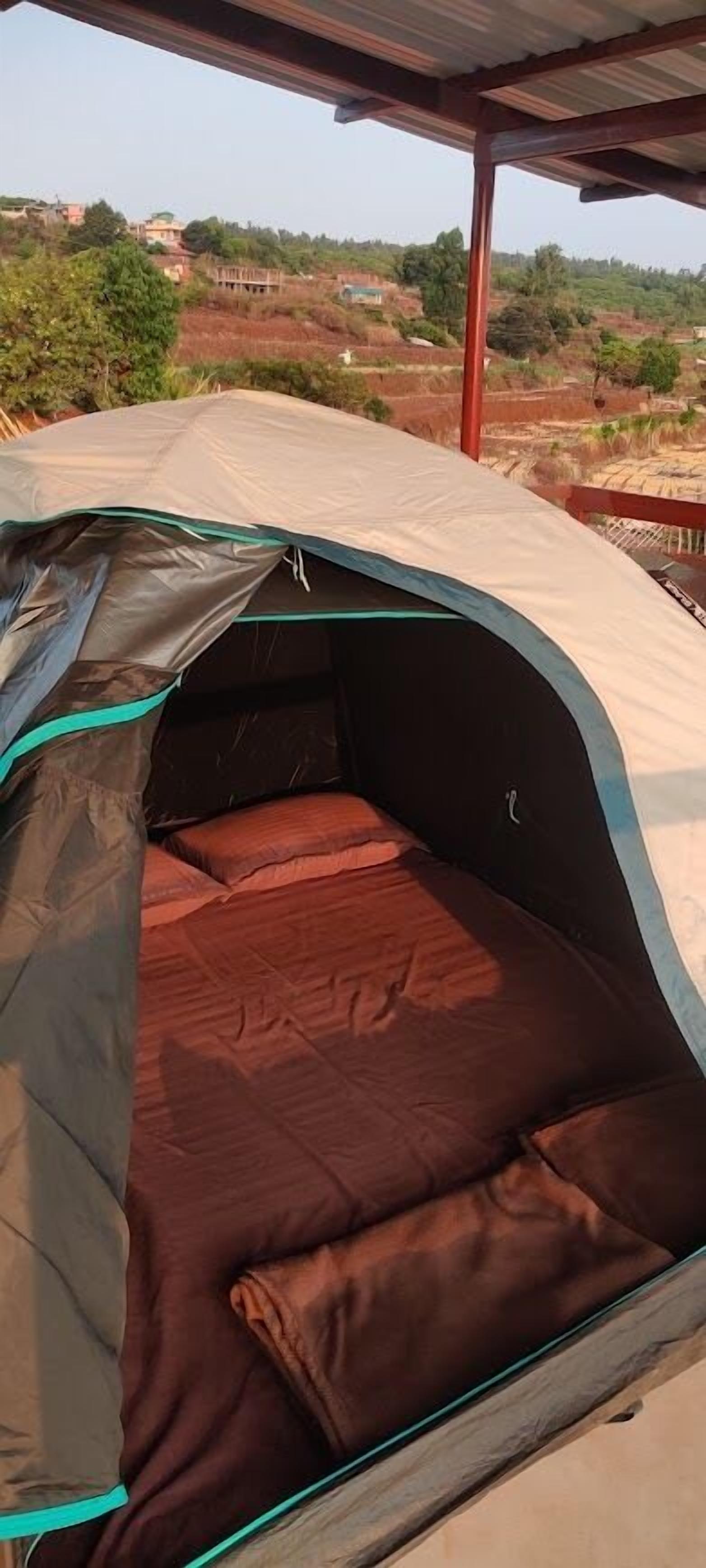 Uma tenda com área de dormir no interior, montada ao ar livre com vista para uma paisagem montanhosa ao fundo.
