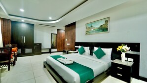 Quarto de hotel com uma cama grande, uma escrivaninha, uma cadeira, um guarda-roupa e um quadro na parede.