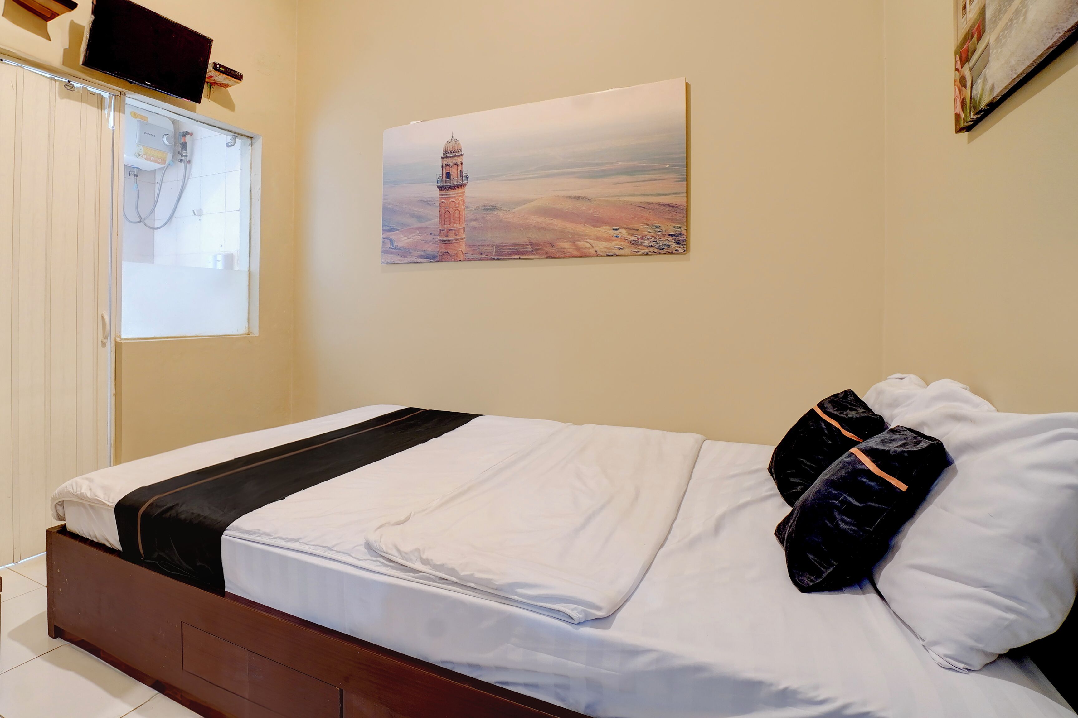 Cama bem arrumada com roupa de cama branca e preta, cabeceira de madeira e um quadro de um farol na parede.