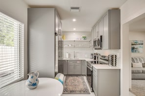 Uma cozinha moderna com armários cinza, bancada branca e um espaço de refeições com mesa e um jarro decorativo.